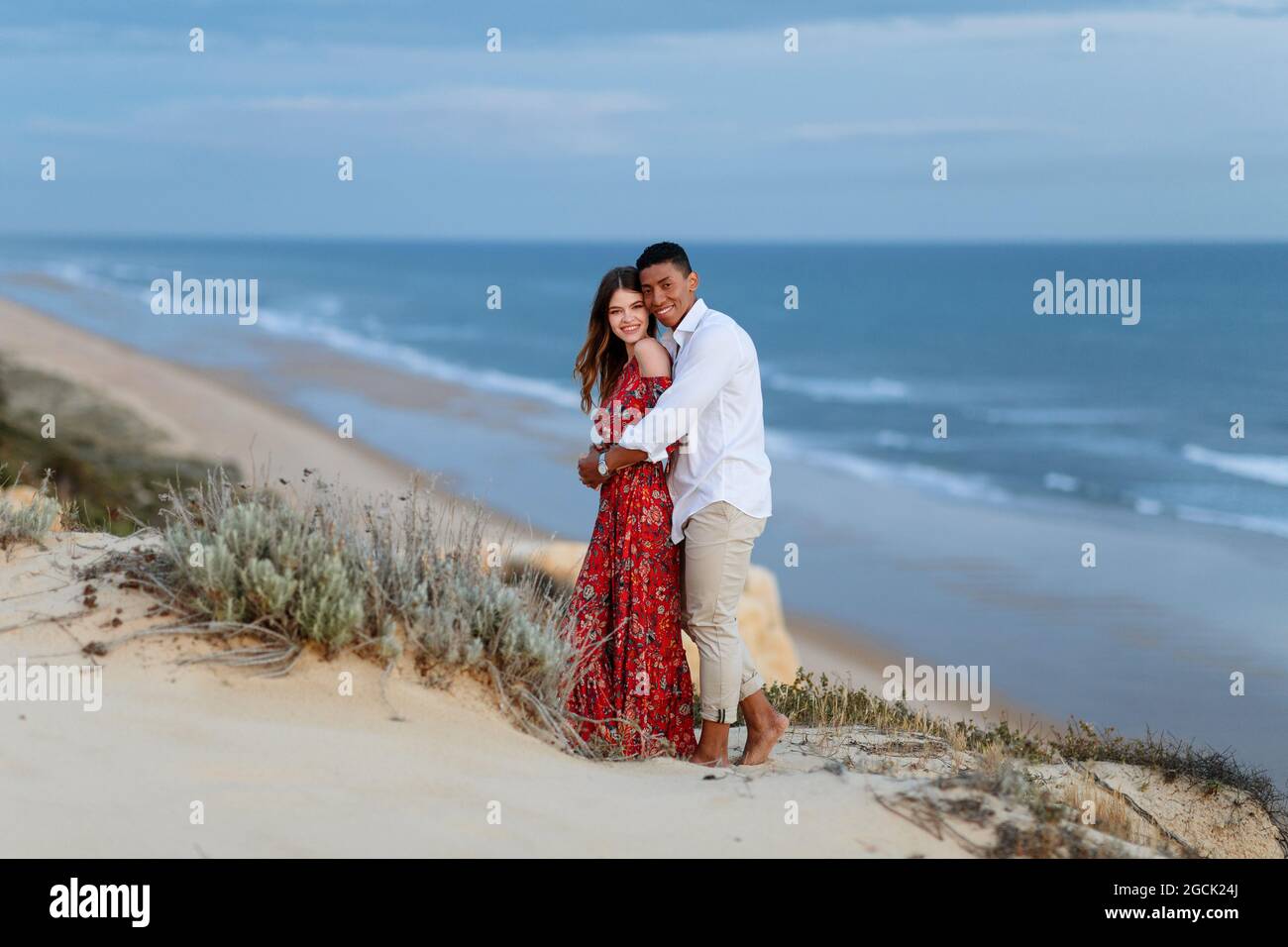 Loving multiracial couple in elegant clothes embracing on hill on ...