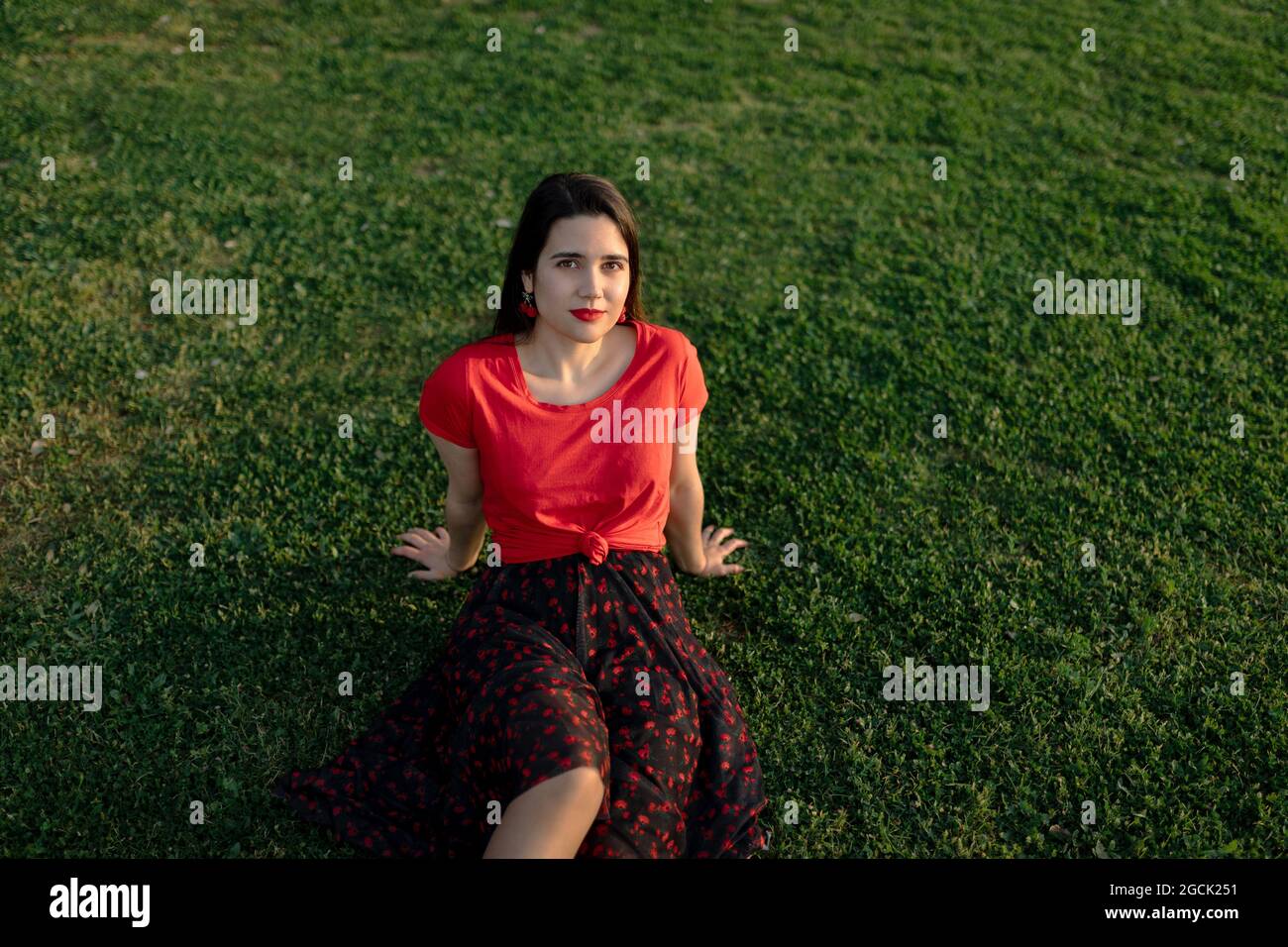 Tranquil female sitting on grass on meadow in park and enjoy sunset in ...
