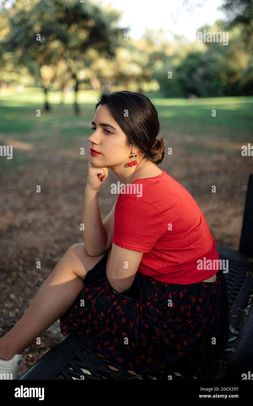 Side view of charming female chilling on bench and looking away while ...