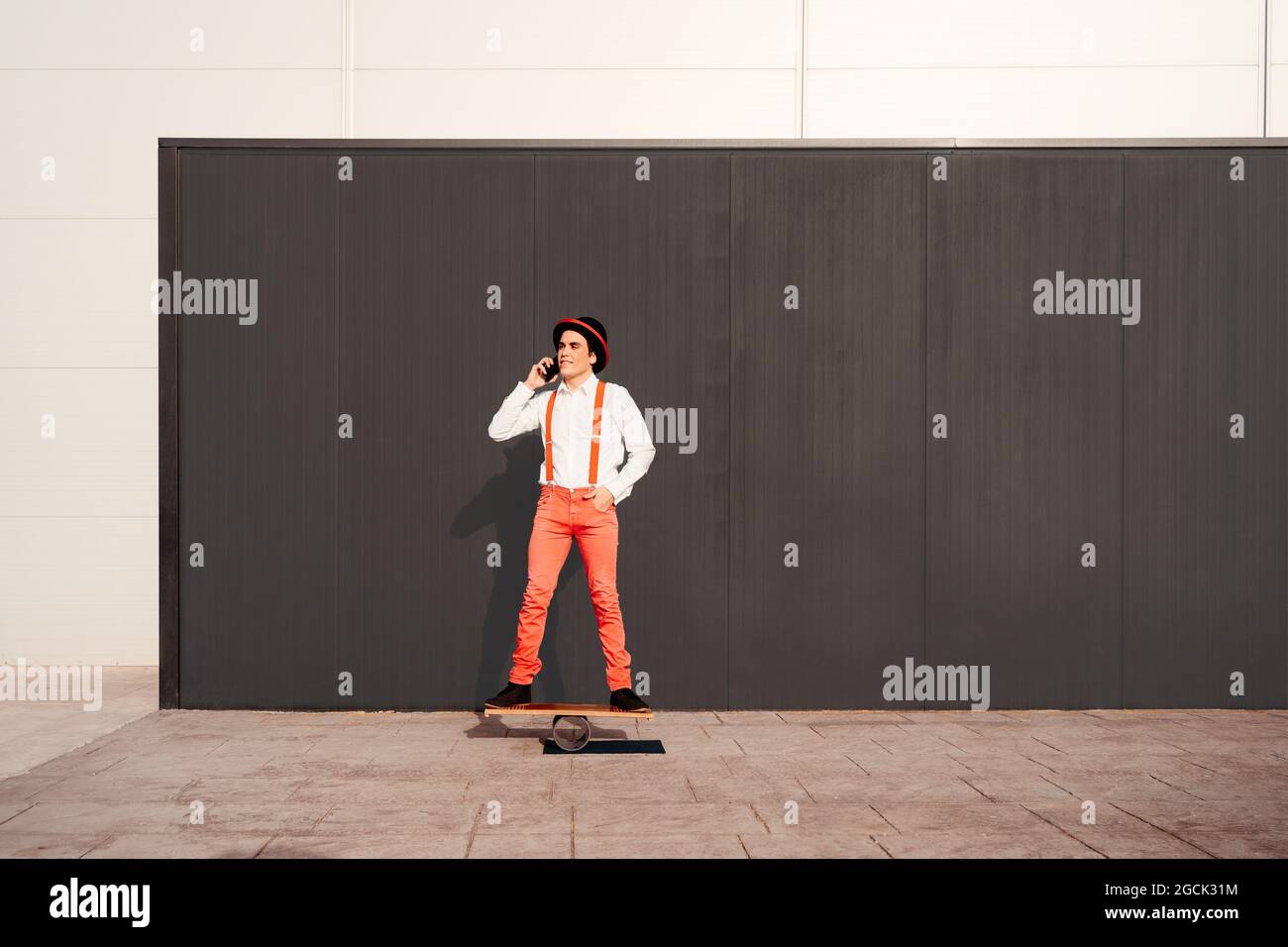 Full body of cheerful young male circus performer talking on smartphone ...