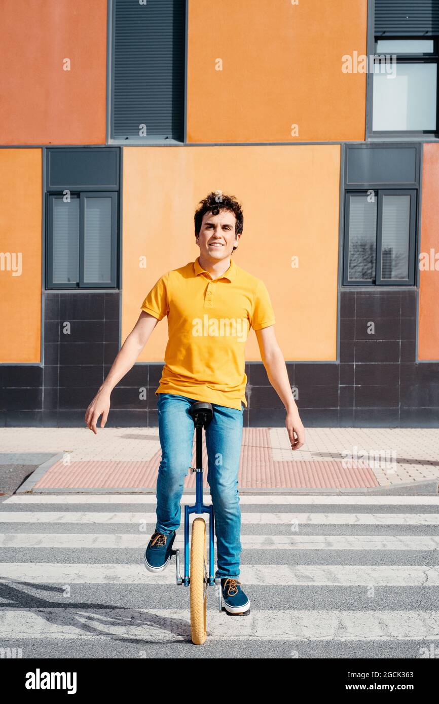 Talented man in casual wear sitting on unicycle crossing road on zebra ...