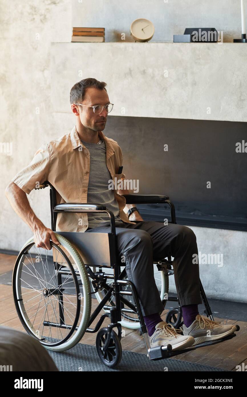 Vertical full length portrait of modern adult man in wheelchair at home ...