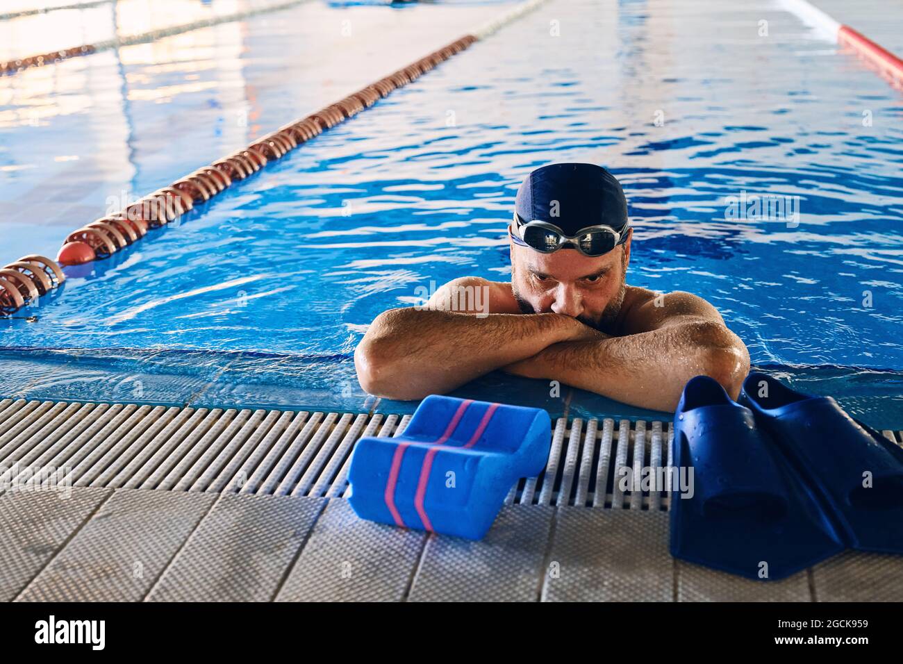 Tired male swimmer leaning on edge of pool and having break during ...