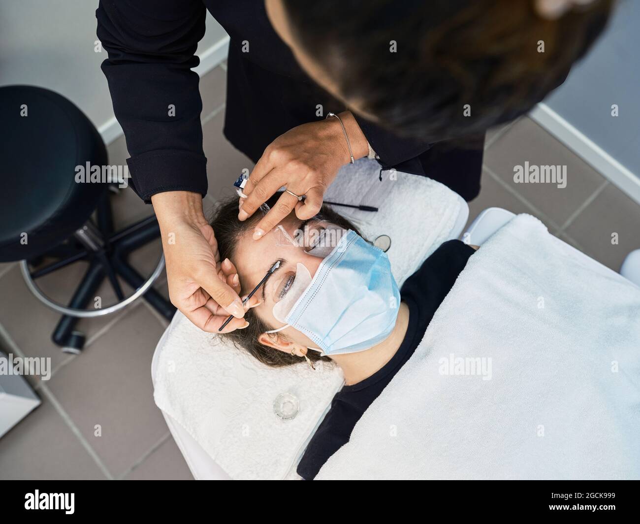 From above crop anonymous beautician with applicator covering eyebrow ...