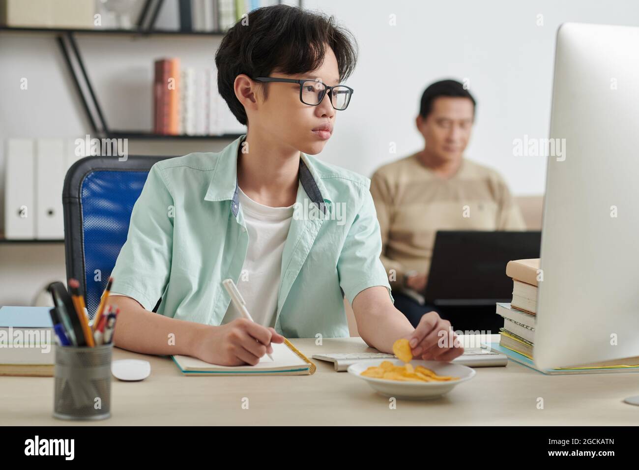 Pensive teenage boy eating potato chips when doing homework on his ...