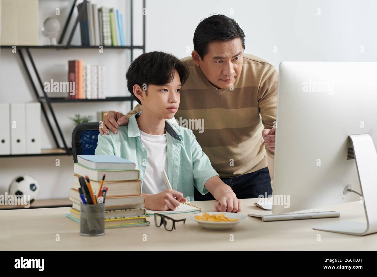 Middle-aged father helping teenage son with doing homework, he is ...