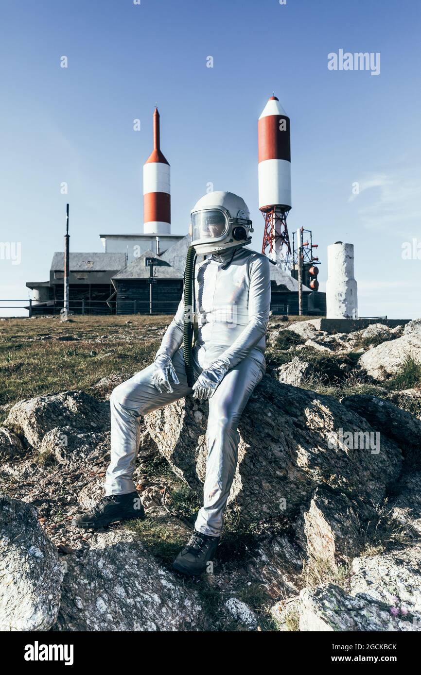 Full body man in spacesuit sitting on rocky ground striped rocket ...