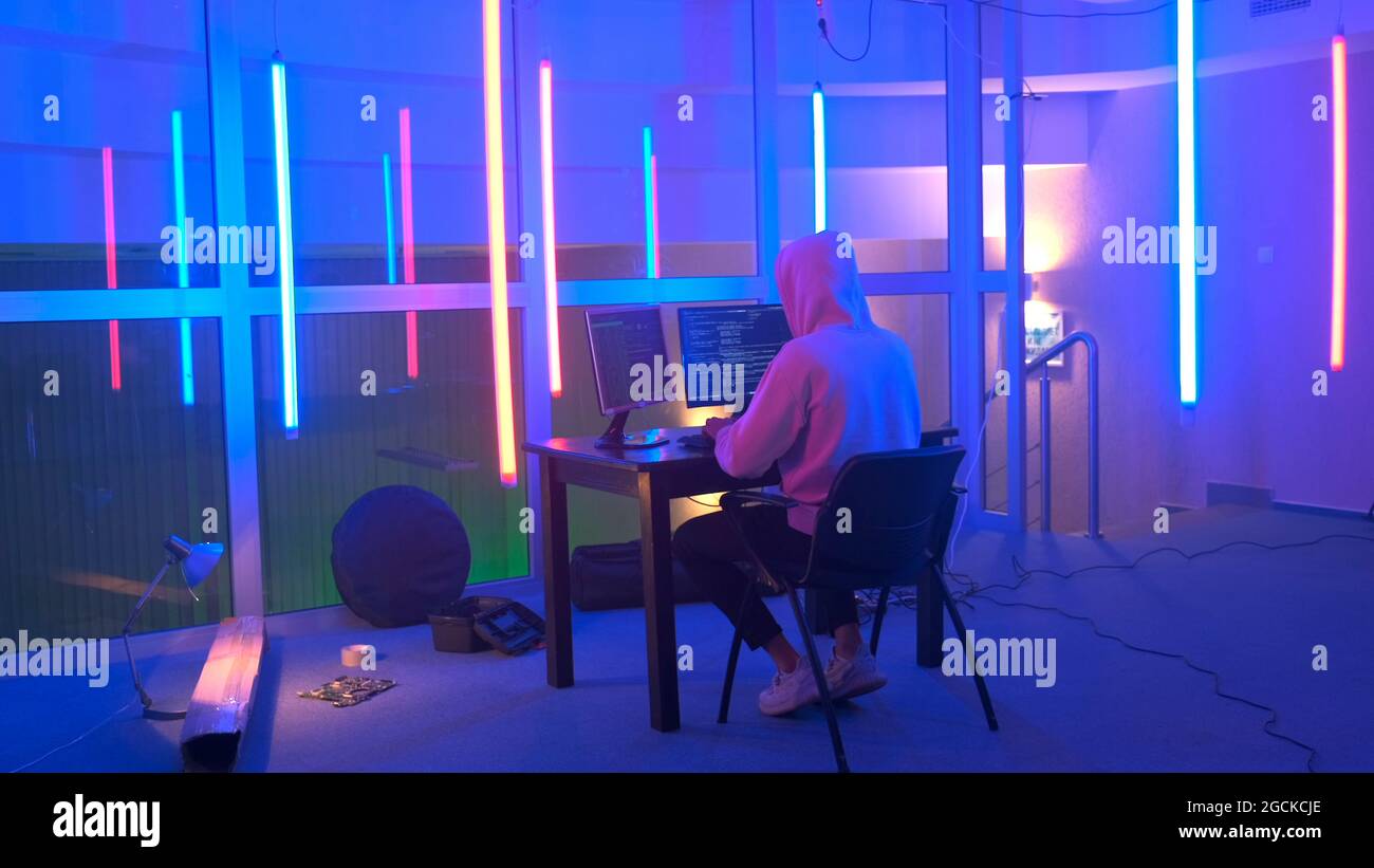 Hacker working place: hacker working in a room with colored neon lights ...