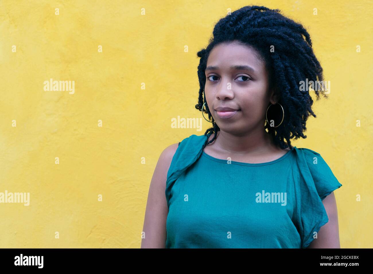 Portrait of young Black Woman with afro hairstyle leaning on a wall ...