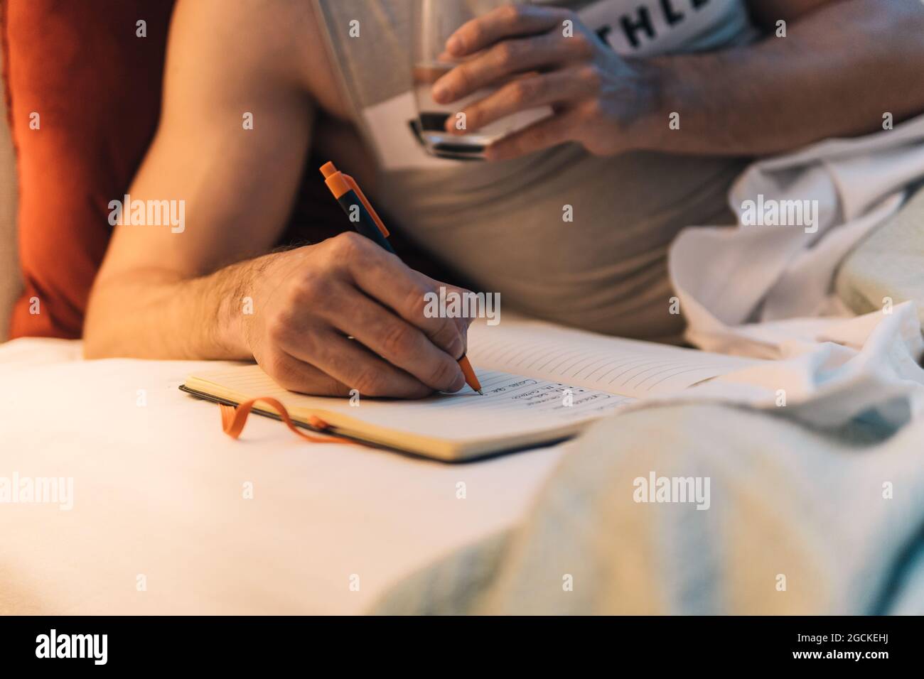 Crop view of male lying in bed and writing in notepad before sleep in ...