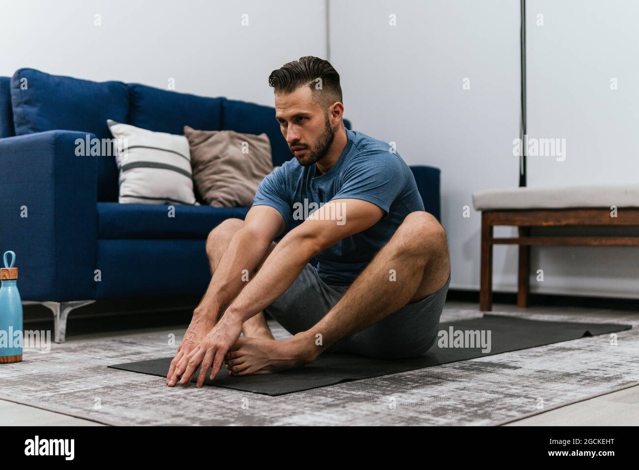 Concentrated athletic male doing stretch exercises near sofa while ...