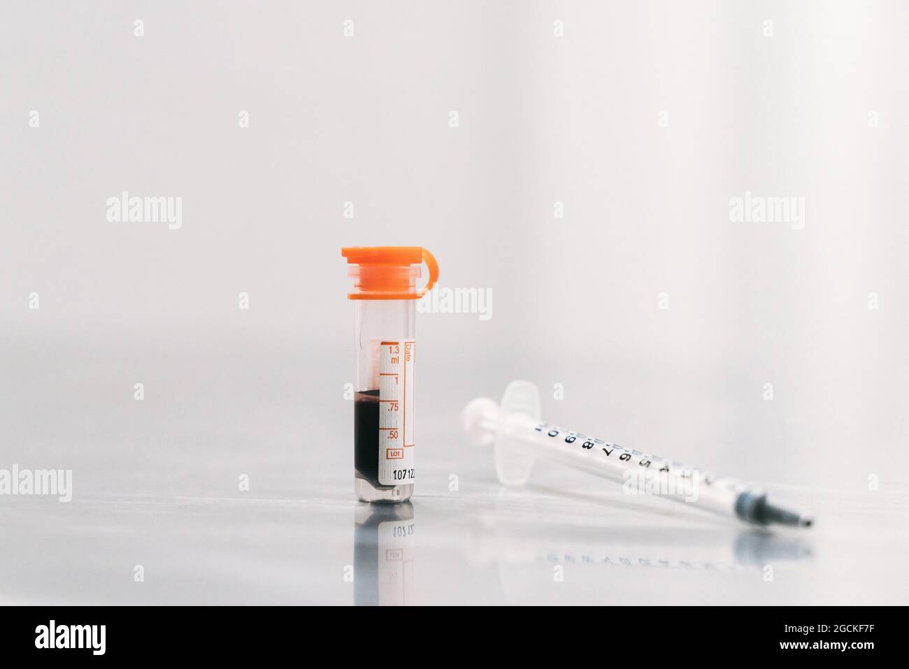 Glass tube with blood sample of patient placed near syringe on table in ...