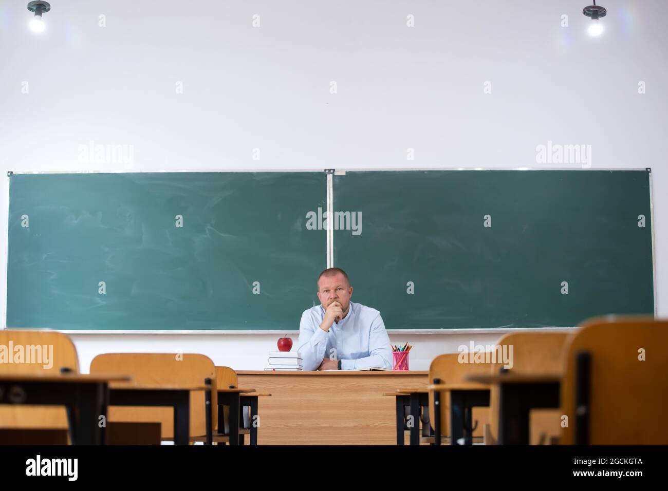 Exhausted teacher in the classroom in fron of the blackboard. Back to ...