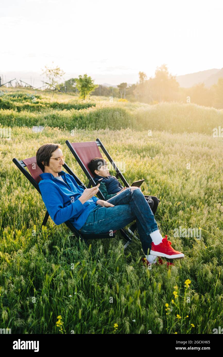 Side view of father and son relaxing in folding hammocks in the middle ...