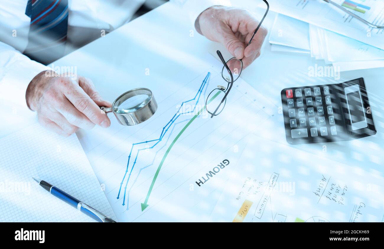 Businessman holding a magnifying glass over a graph showing growth ...