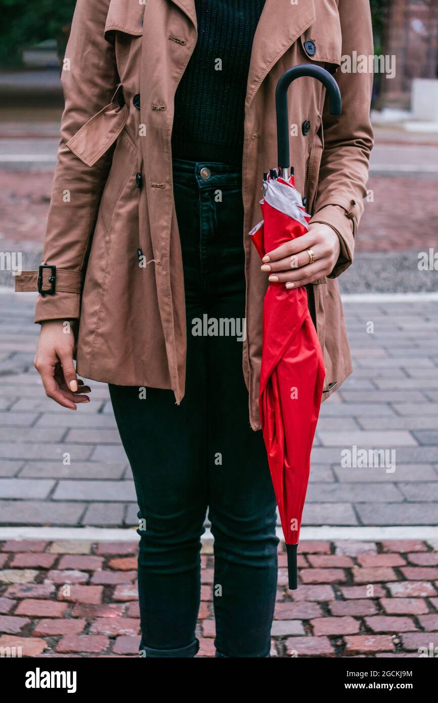 Anonymous female in casual clothes and with umbrella standing on paved ...