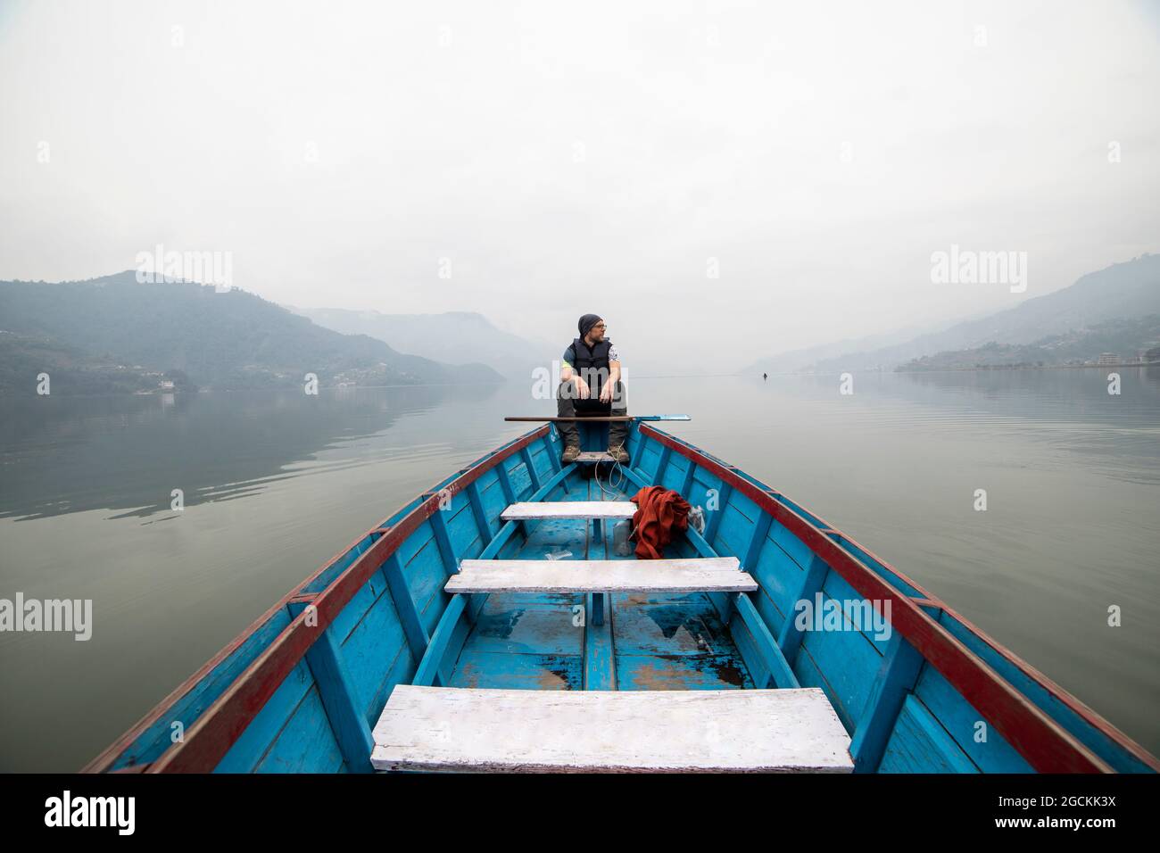 Male explorer floating in blue wooden boat on calm lake in misty ...