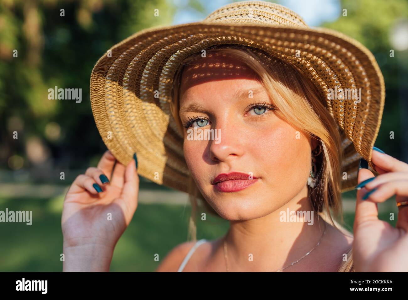 Charming female wearing straw hat looking at camera on sunny day in city street in summer Stock ...