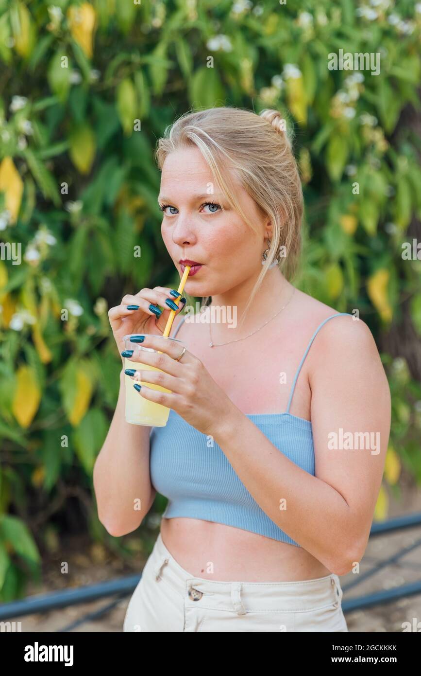 Charming female drinking cold refreshing lemonade with straw while ...