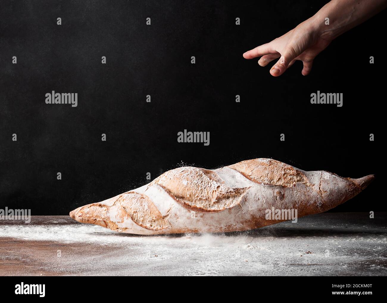 Crop anonymous baker dropping baked bread dusted with flour on the ...