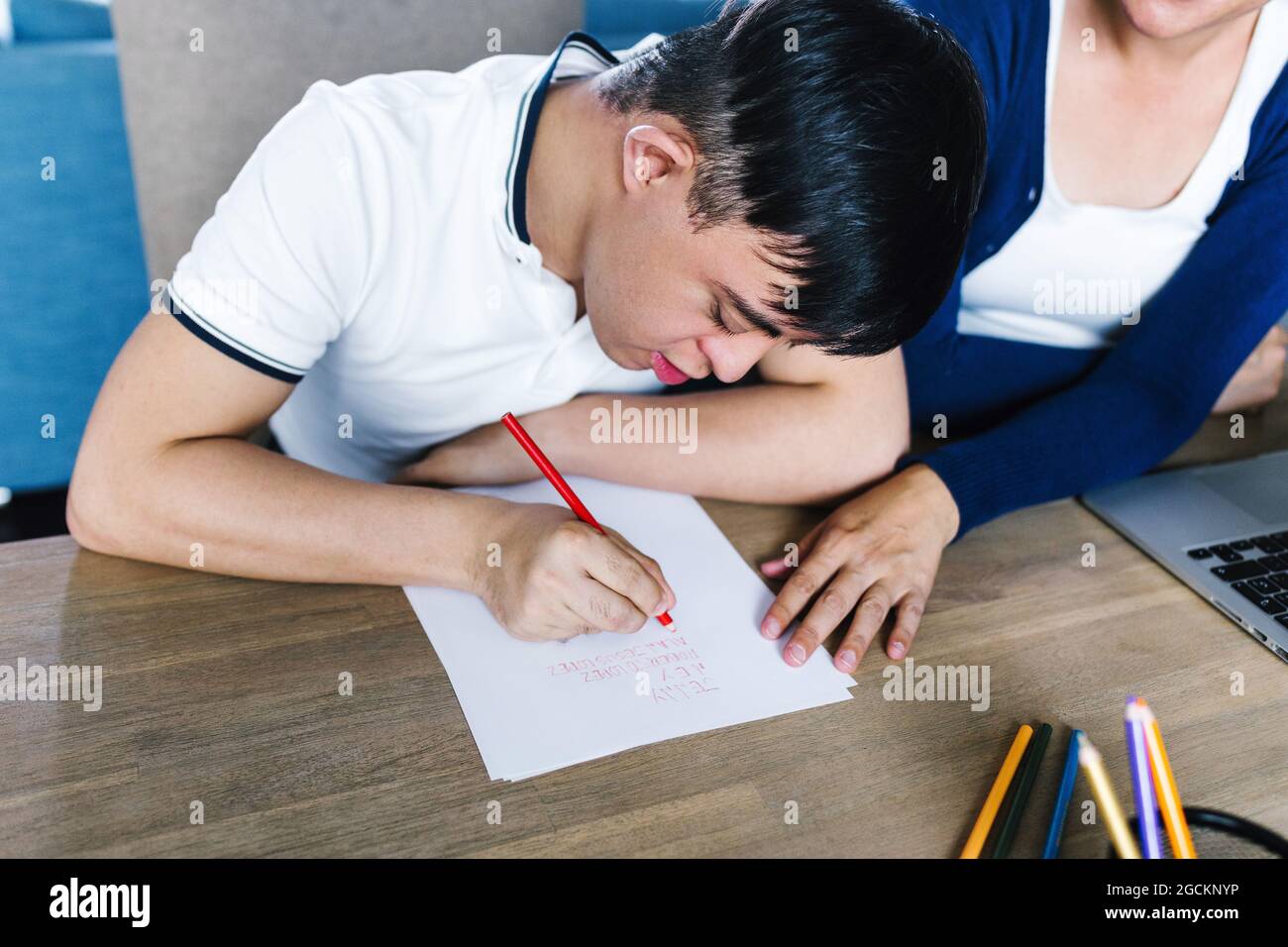 Ethnic teenage boy with Down syndrome drawing with pencils on paper ...