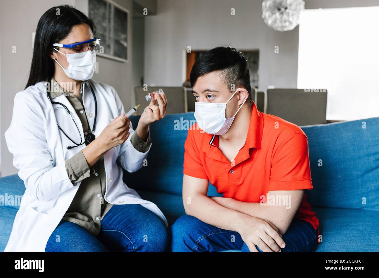 Female medic in protective uniform filling syringe with vaccine while ...