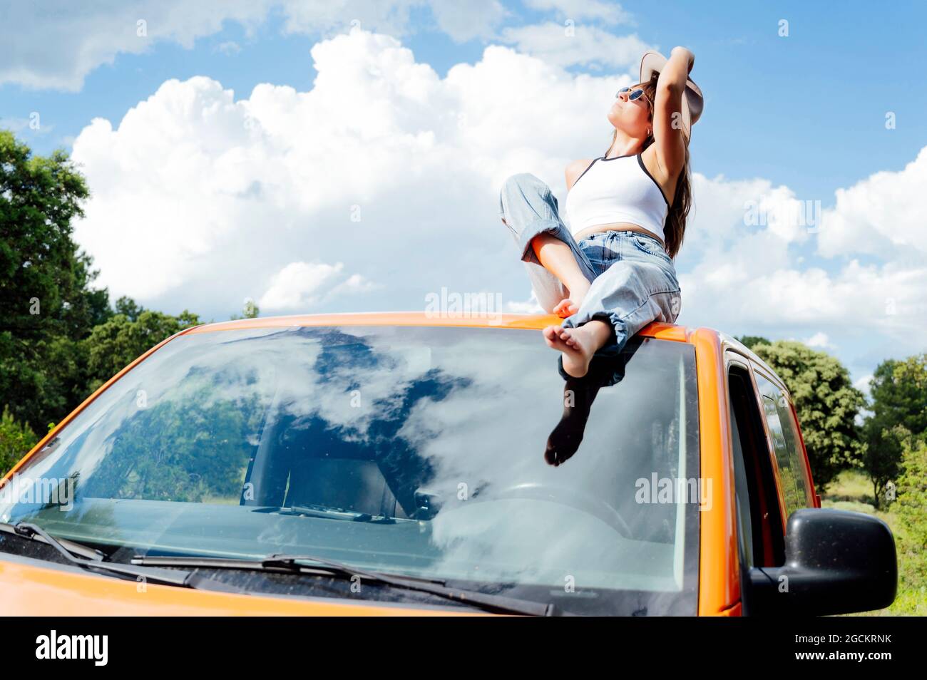Serene female explorer sitting on roof of van and enjoying summer ...