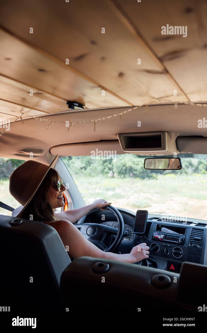Side view of female traveler sitting on driver seat in van and enjoying ...