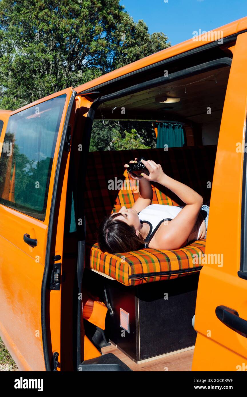 Side view of female traveler lying in van and looking through taken ...