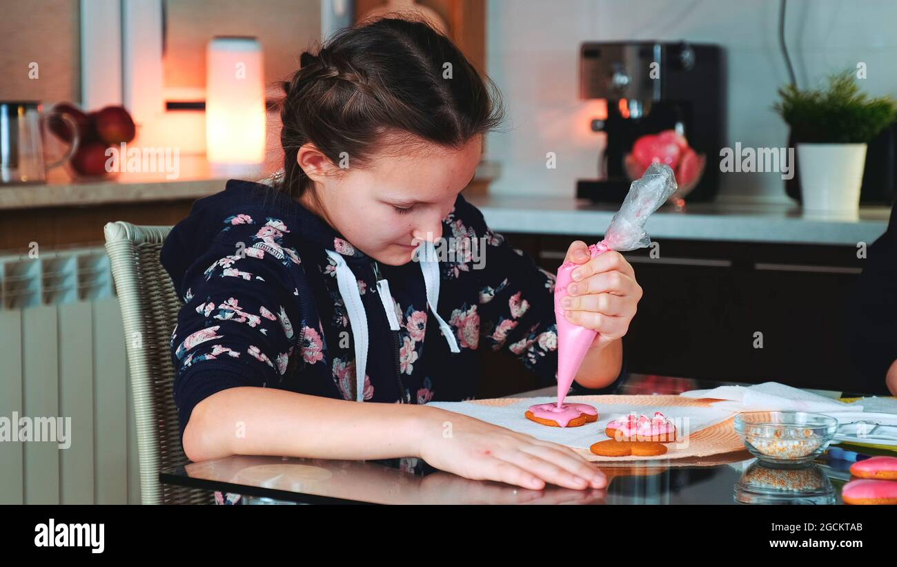 Pretty girl decorating cookies with color sugar glaze in the evening at ...