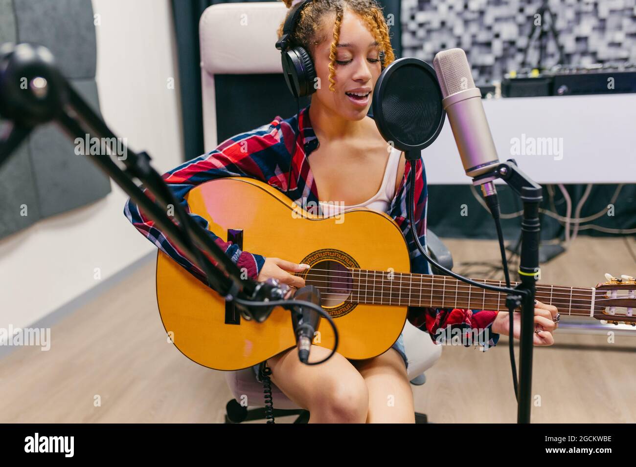 Young ethnic female vocalist in headphones playing acoustic guitar ...