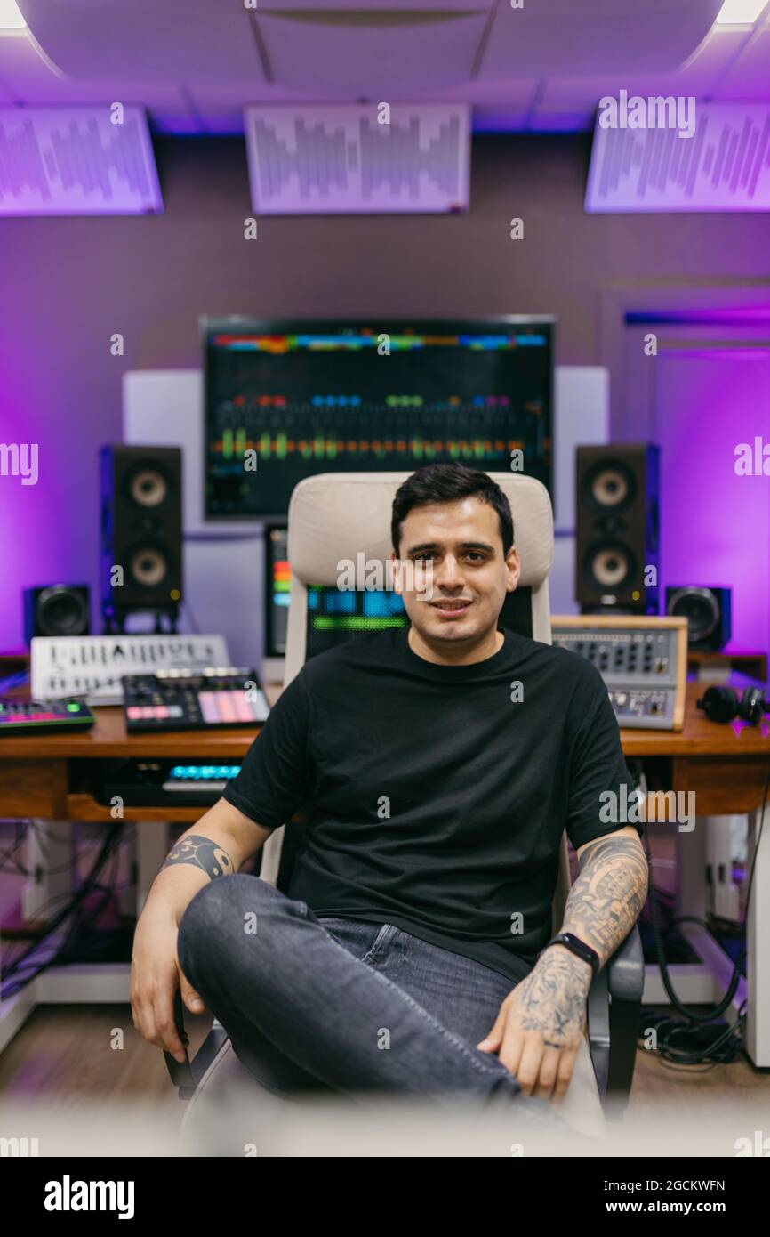 Confident male sound engineer sitting with crossed legs in armchair ...