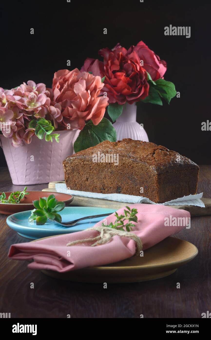 Still life of a sponge cake next to some pink vases with flowers on a ...