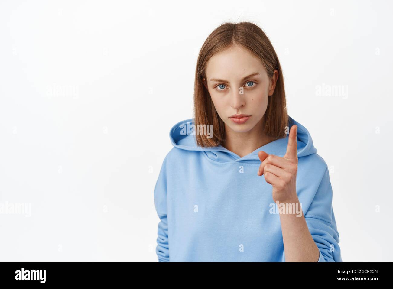 I warn you. Serious young blond girl shaking finger and looking at ...