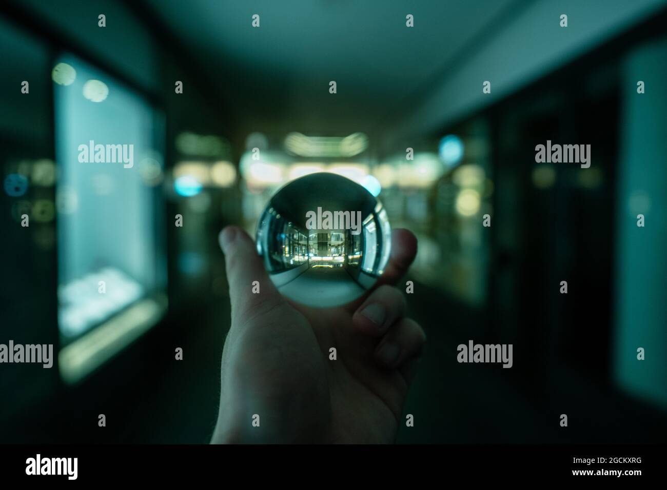 Closeup of a hand holding a glass ball with shop windows reflection ...