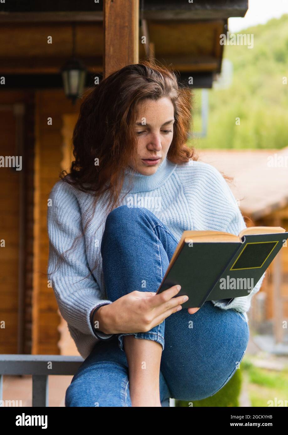 Thoughtful female sitting on terrace with interesting book during ...