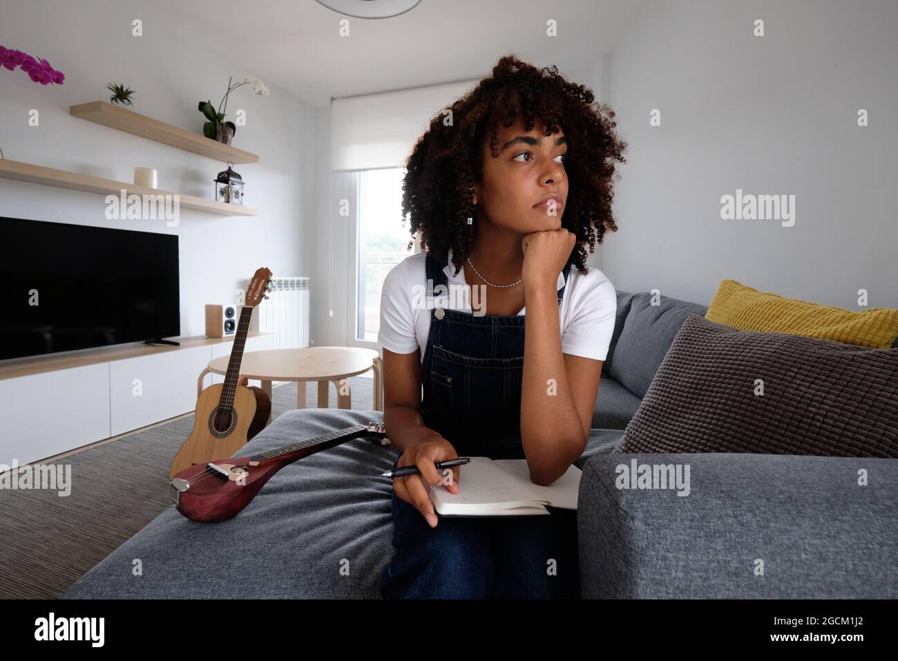 Thoughtful African American female musician sitting on bed with ...
