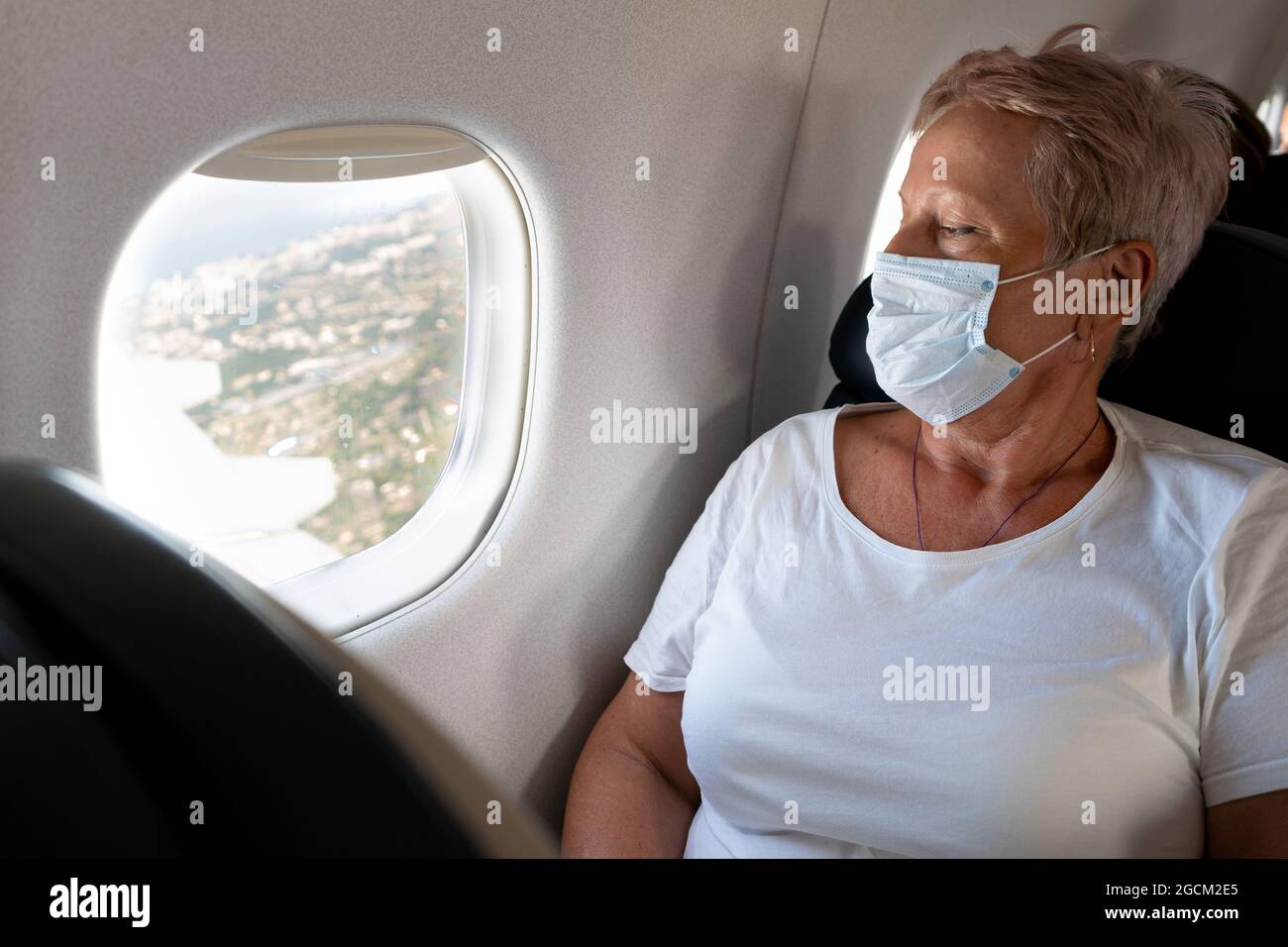 An elderly woman travels. Flying in a plane wearing a mask. Passenger ...