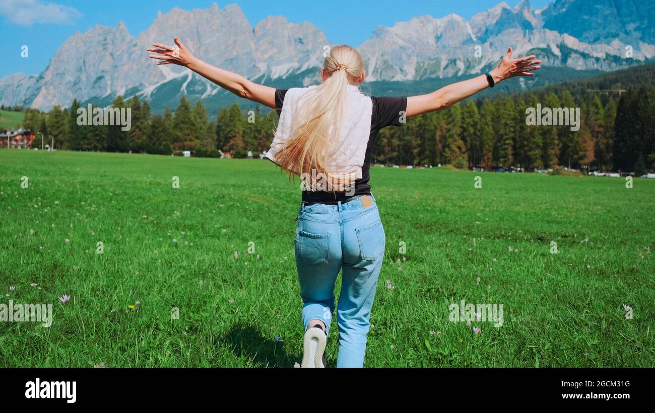 Back view of woman running on the field with mountains in front ...