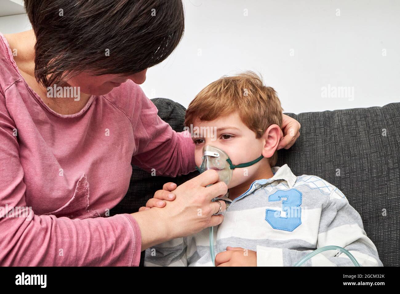Content mother putting on oxygen mask on face of son for inhalation ...