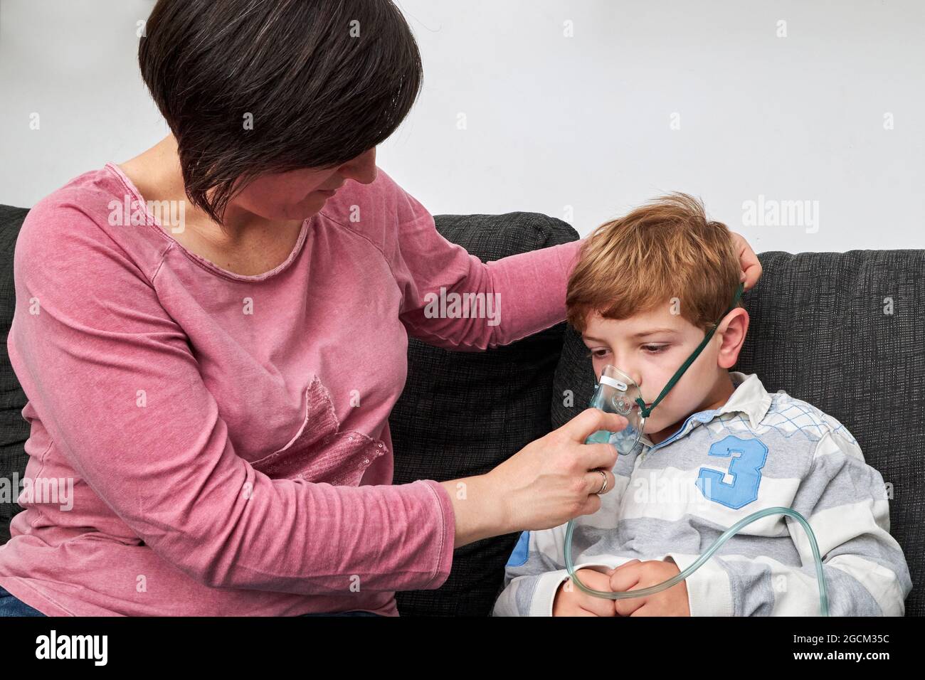 Content mother putting on oxygen mask on face of son for inhalation ...