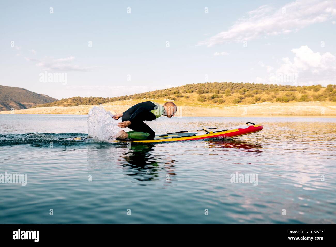 Full body side view of adult male in wetsuit kneeling on paddle board ...