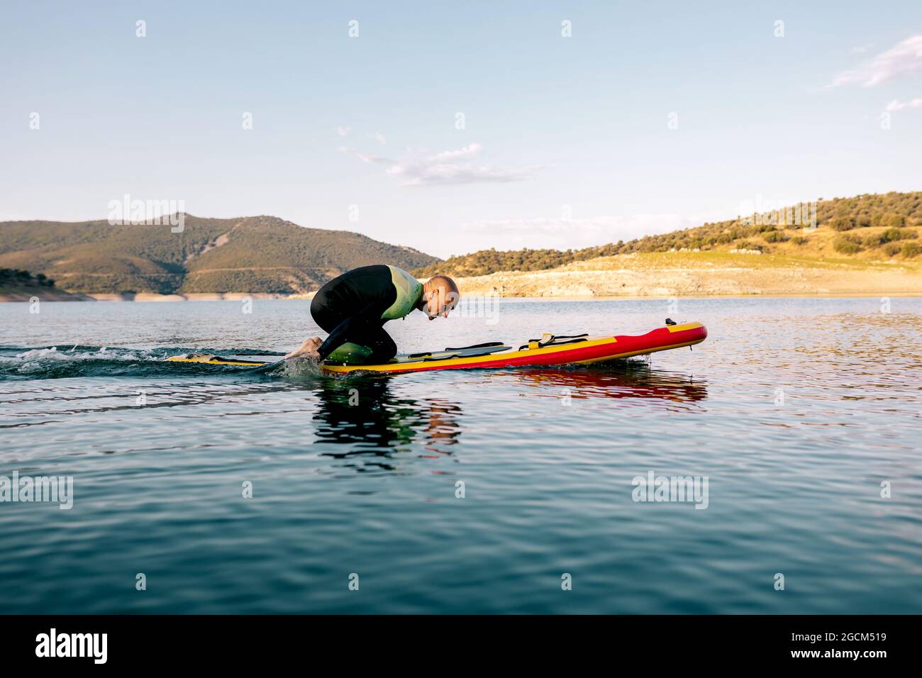 Full body side view of adult male in wetsuit kneeling on paddle board ...
