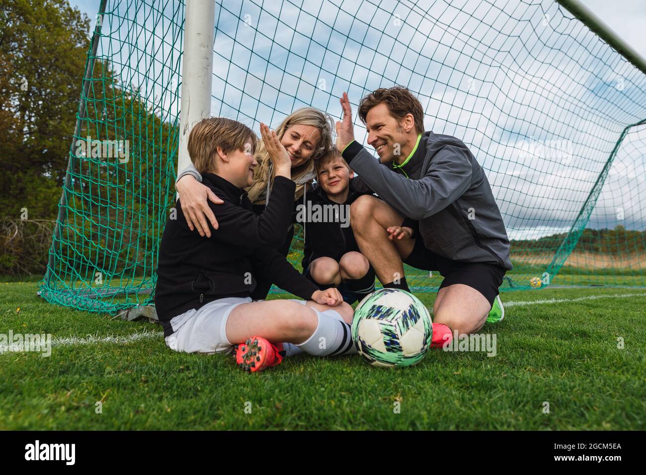 Bonding family in sportswear giving high five while gathering in green ...