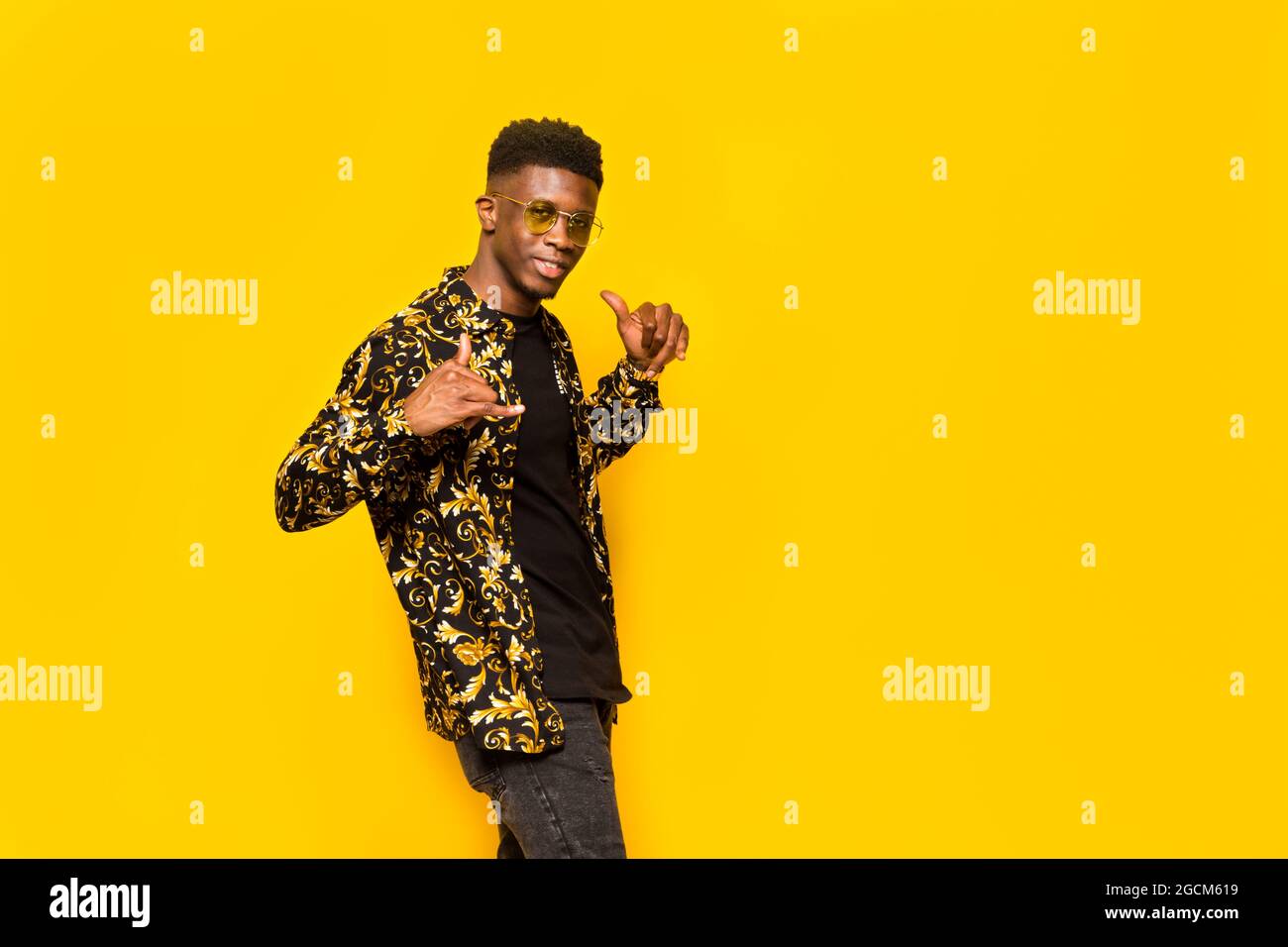 Smiling African American male in trendy outfit showing shaka gesture on ...