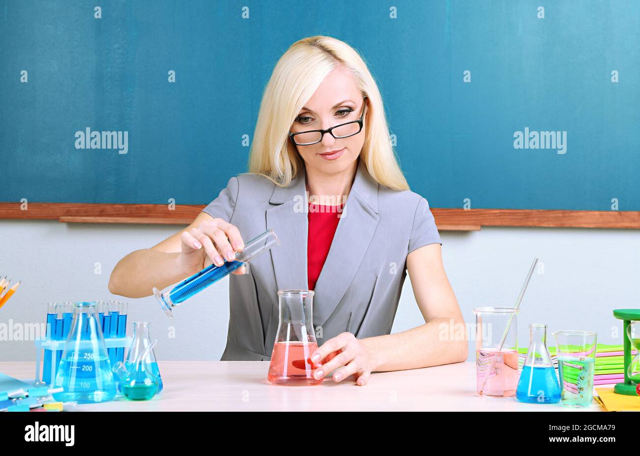 Chemistry teacher with tubes sitting at table on blackboard background ...