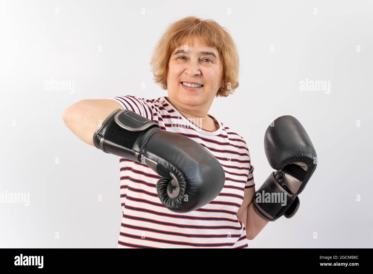Elderly woman in fighting gloves in a defensive pose on a white ...