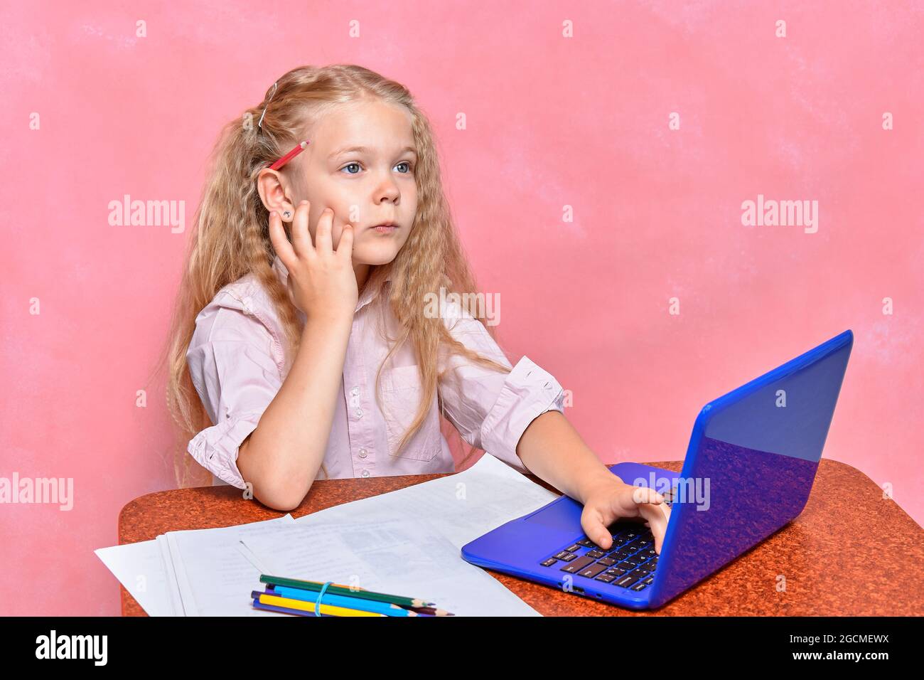 little schoolgirl thoughtful dreaming behind laptop. online training ...