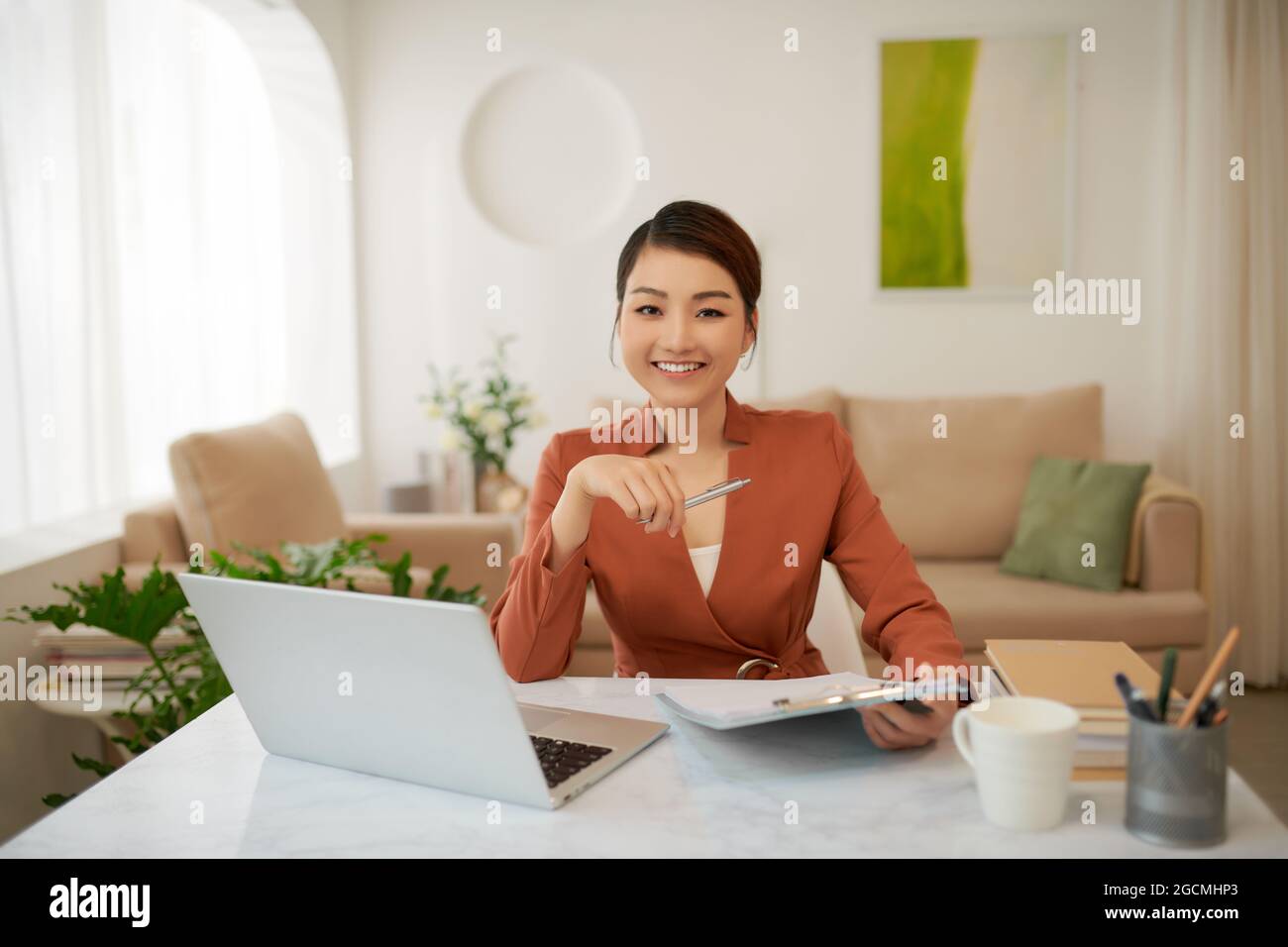 attractive young businesswoman using laptop and smiling at camera while ...
