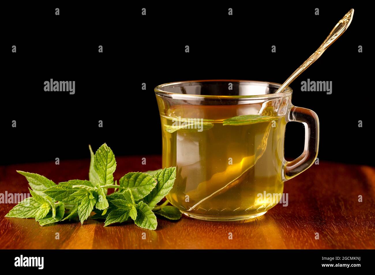 A glass cup of peppermint tea and a pile of fresh peppermint leaves ...